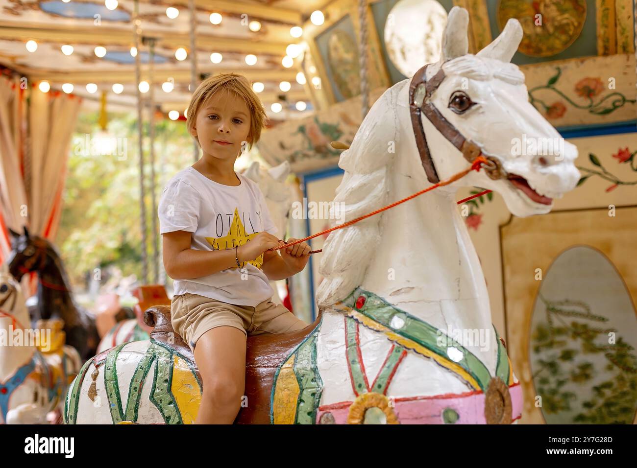 Cute blond child, going on Merry Go Round, kid play on carousel park ...