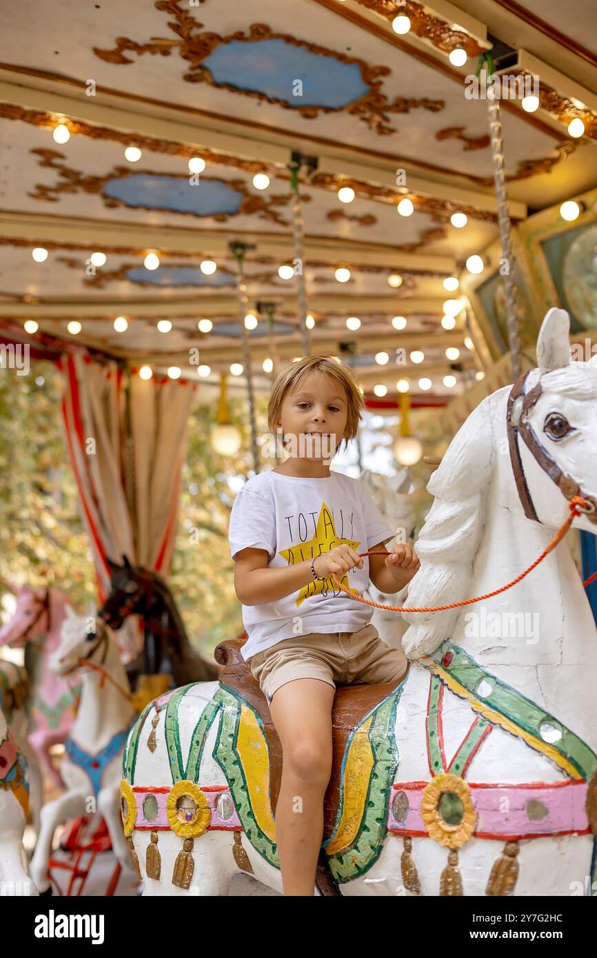 Cute blond child, going on Merry Go Round, kid play on carousel park ...