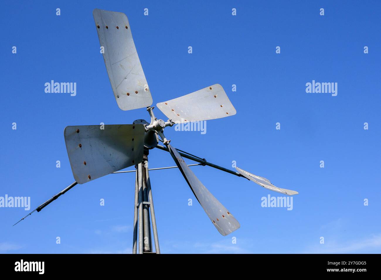 A small windmill providing wind energy on a farm, against a clear blue ...