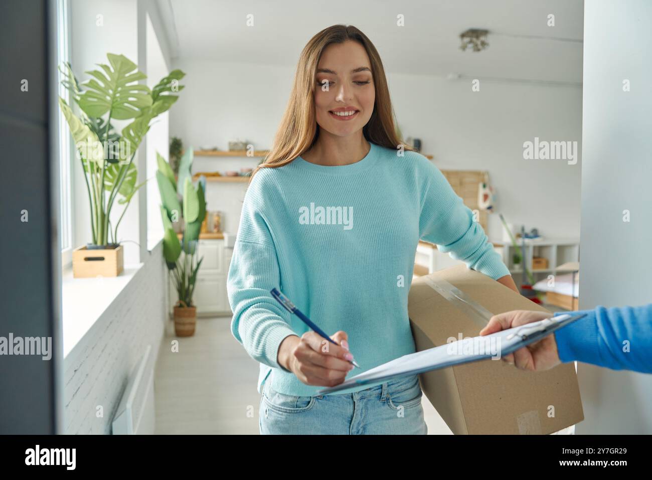Happy young woman accepting box from delivery man and signing paper ...