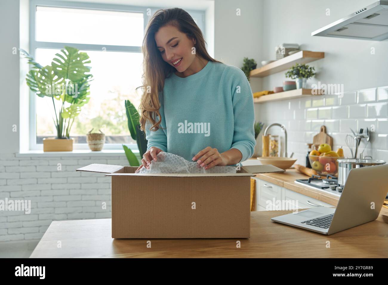 Attractive young woman unpacking box while standing at the domestic ...