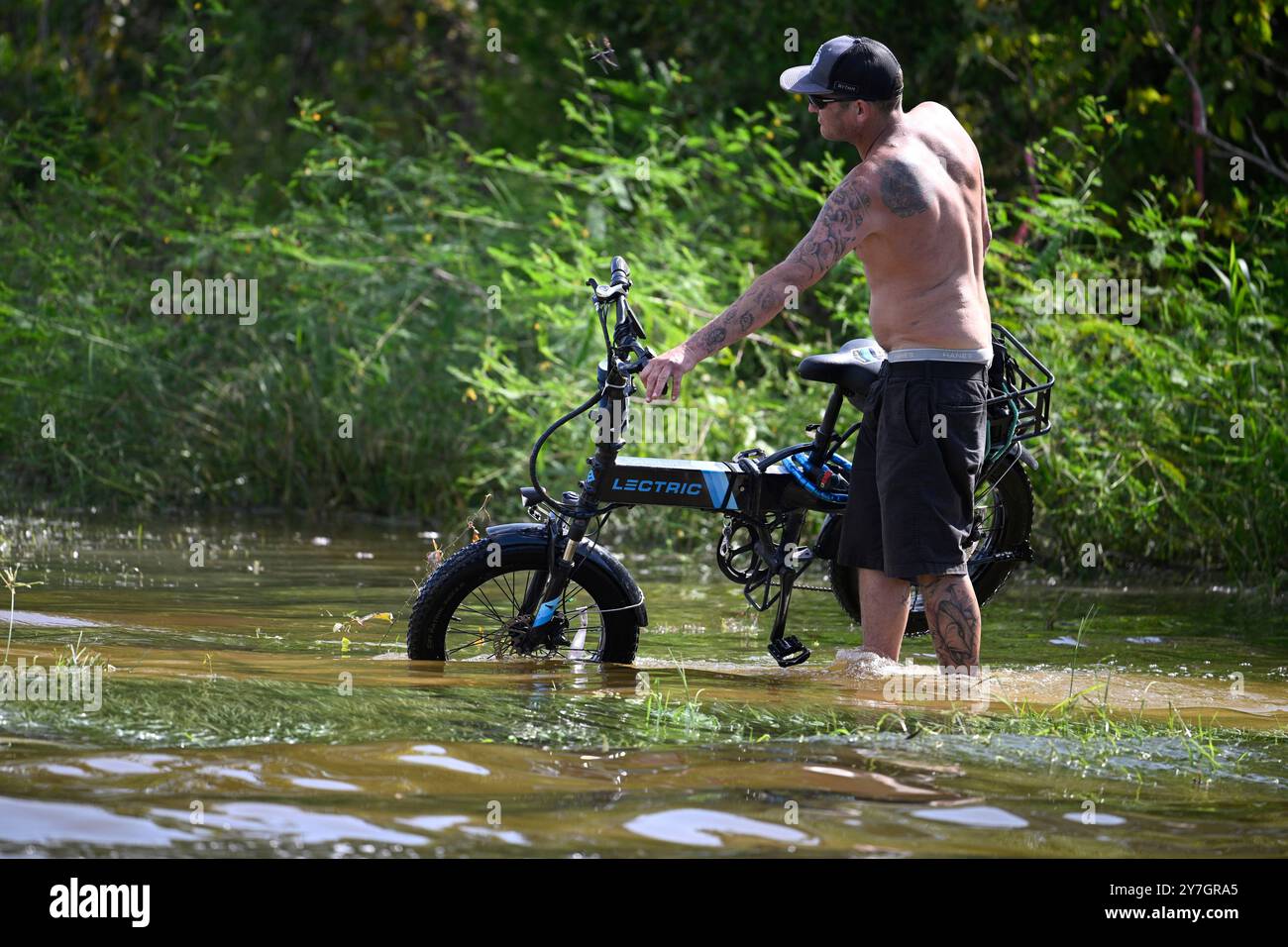 A man carries his electric bicycle through a flooded street in the ...