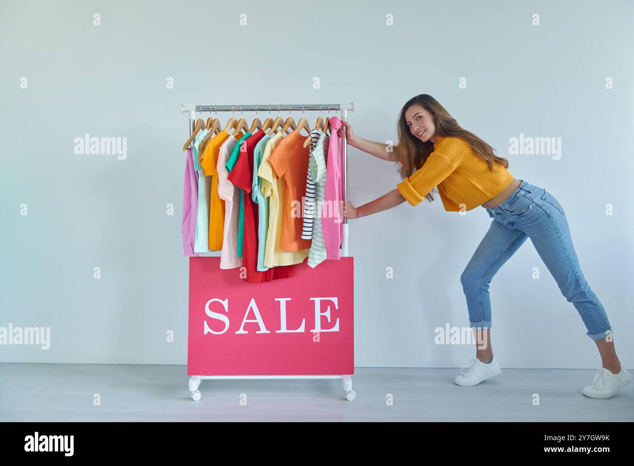 Beautiful young woman pulling a rack with colorful clothes Stock Photo ...