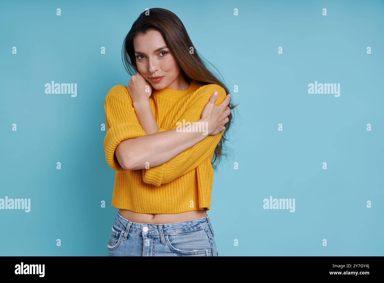 Beautiful young woman hugging self while standing against blue ...