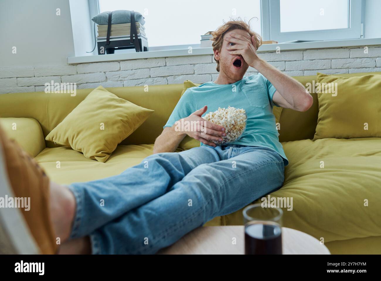Shocked young man watching scary movie while sitting on the couch at ...