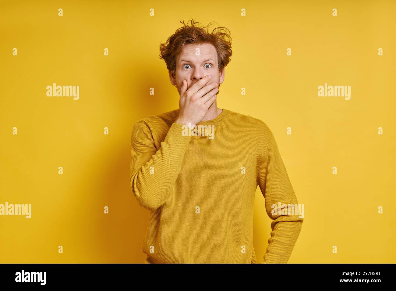 Shocked redhead man covering mouth with hand while standing against ...
