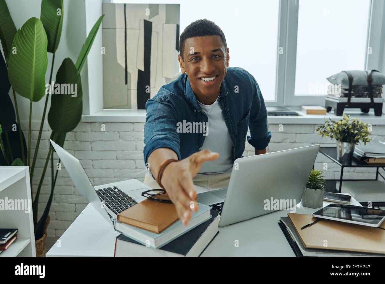 Cheerful young mixed race man reaching out hand for handshake while ...