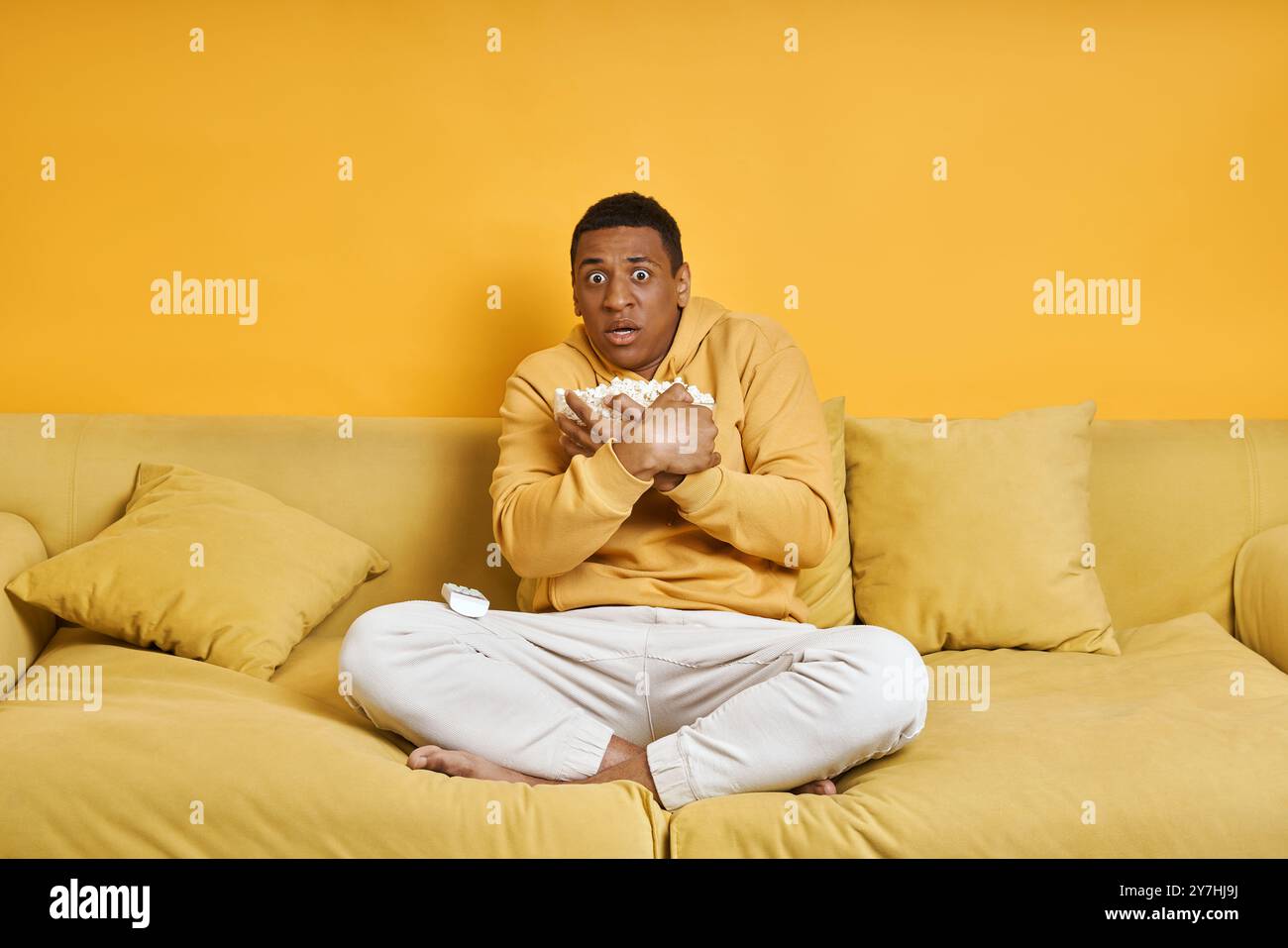 Terrified man holding plate with popcorn while sitting on the couch ...