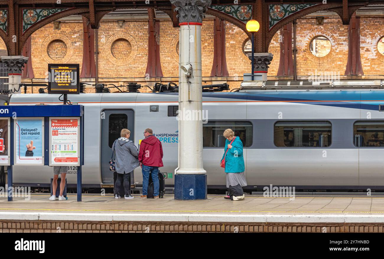 A modern train stands at a historic railway station platform under a ...