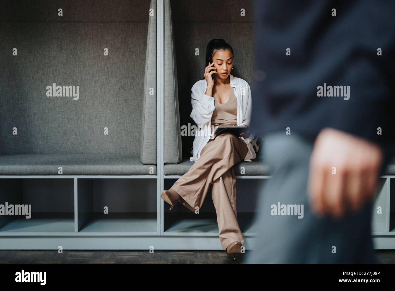 Female entrepreneur talking on smart phone while sitting with legs crossed in booth at office ...