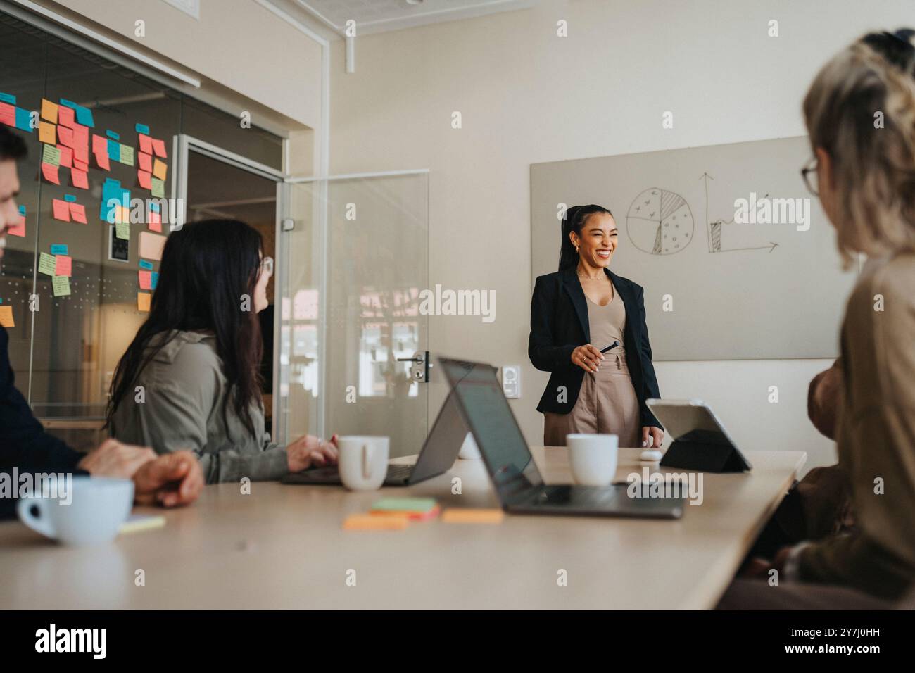 Smiling young businesswoman explaining ideas to coworkers at meeting ...