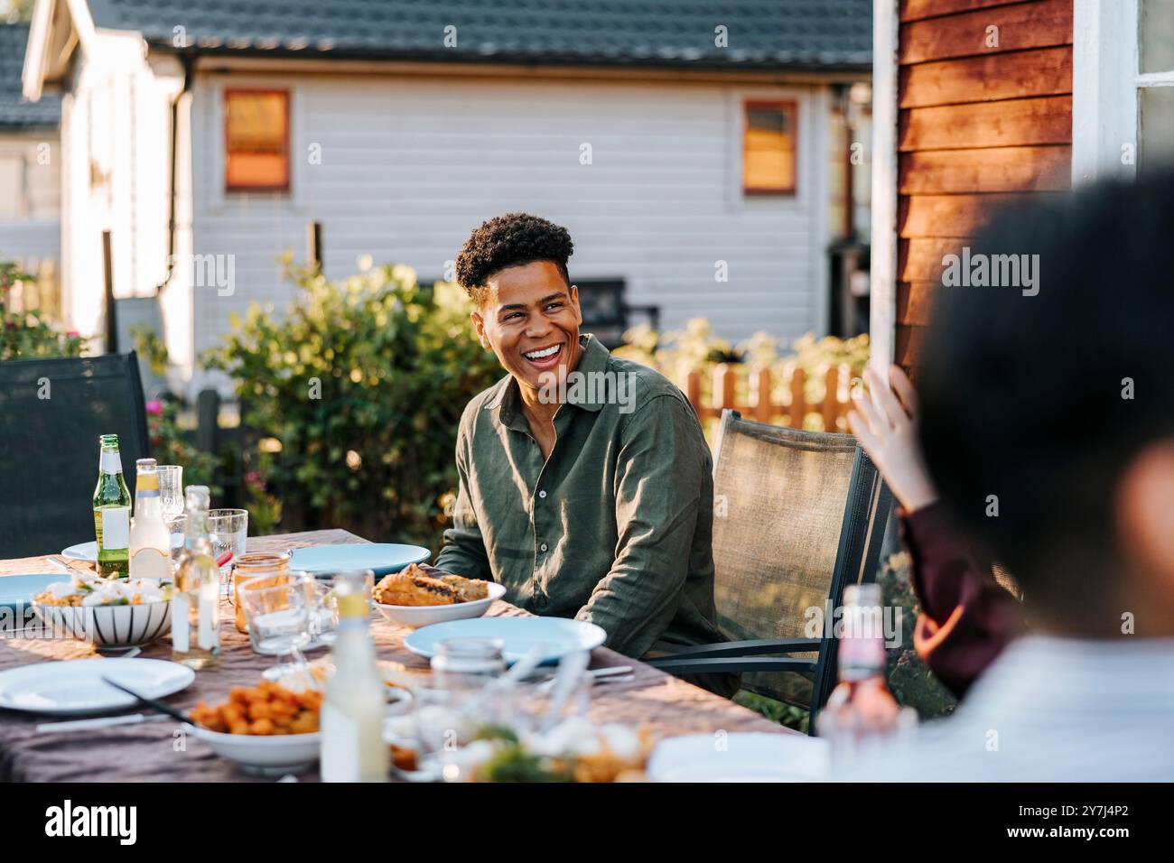 Happy young man sitting on chair near dining table in back yard at ...