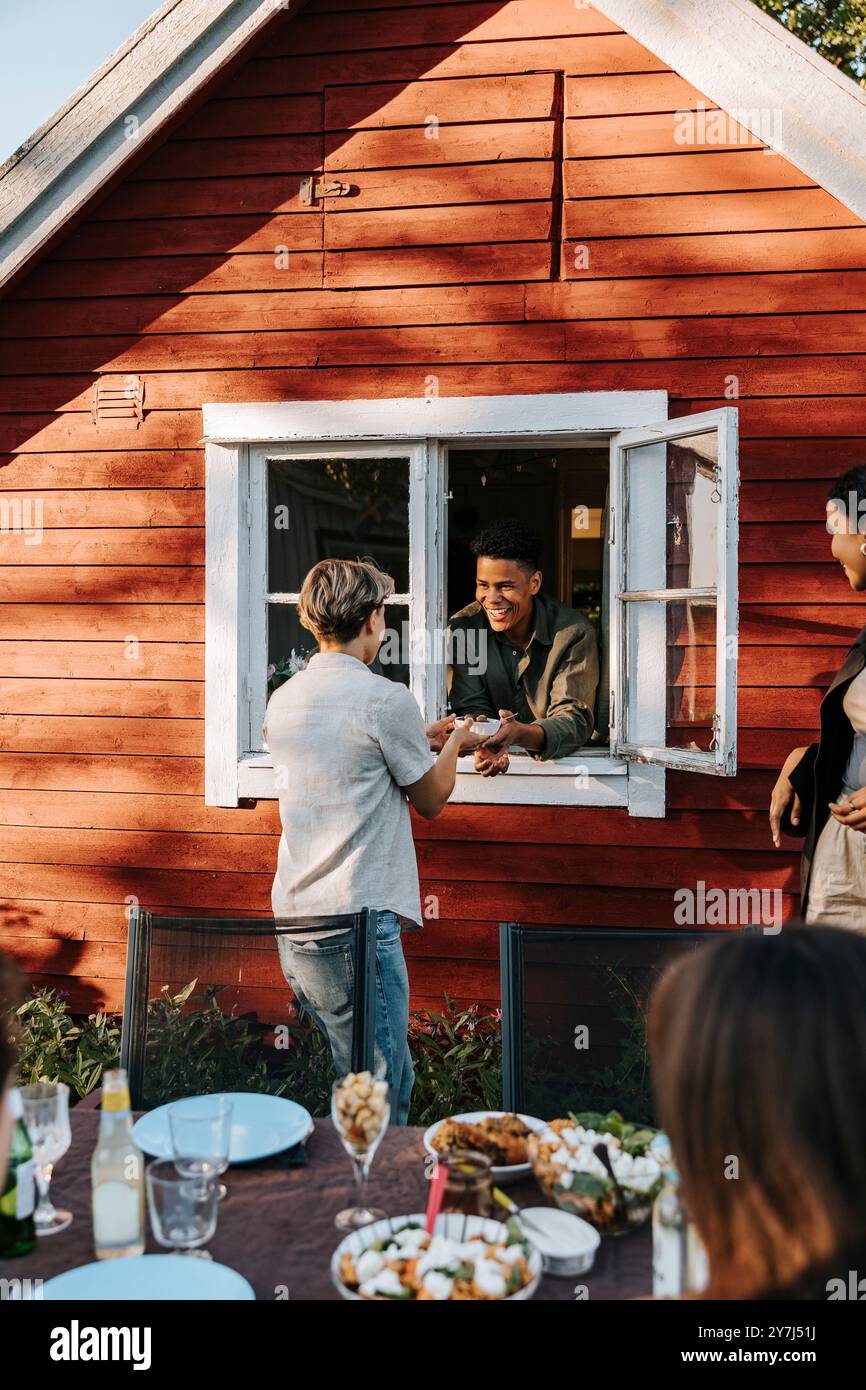 Happy young man passing food through window to female friend standing ...