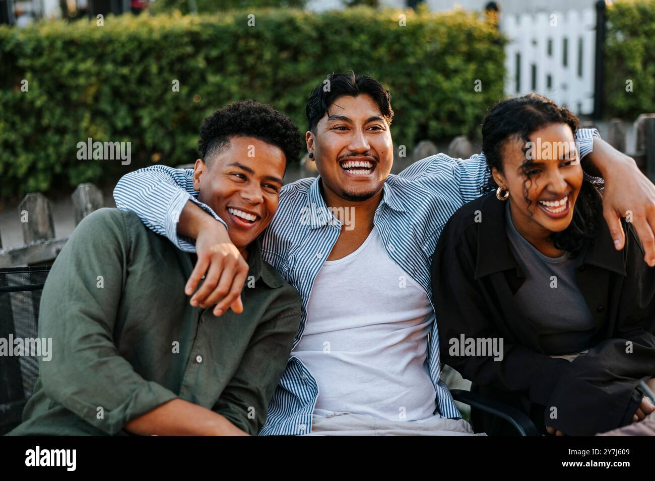 Happy young man with arm around male and female friend enjoying in back ...