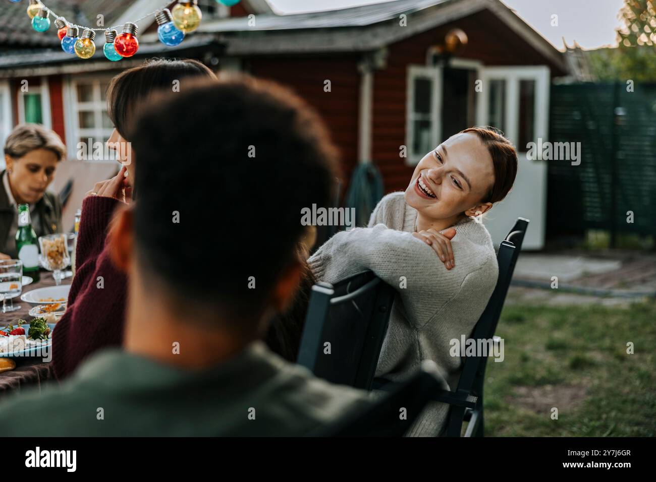 Happy young woman leaning on chair while talking with male friend in ...