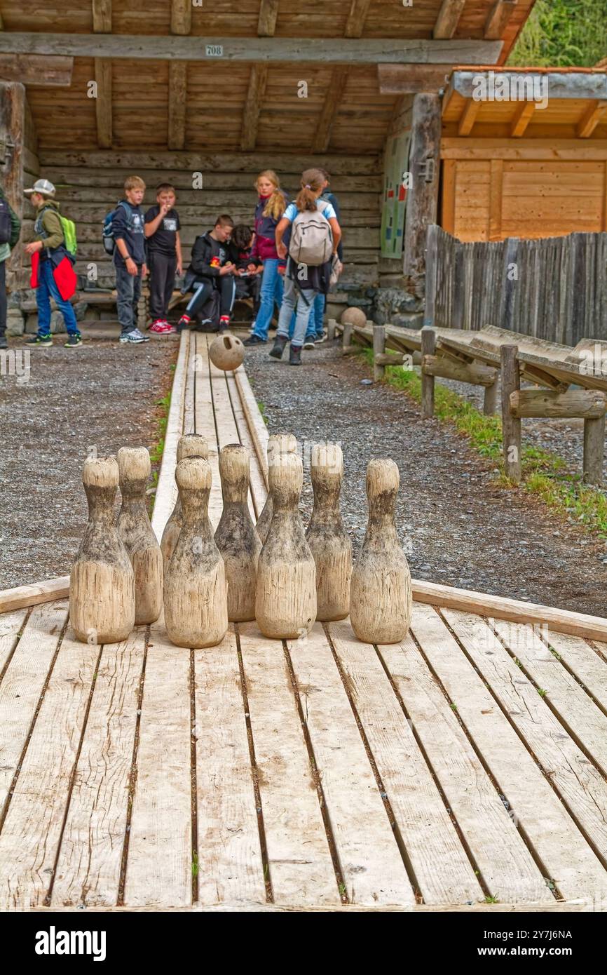 wood bowling set, ball in motion, wooden platform, outdoors, teens ...