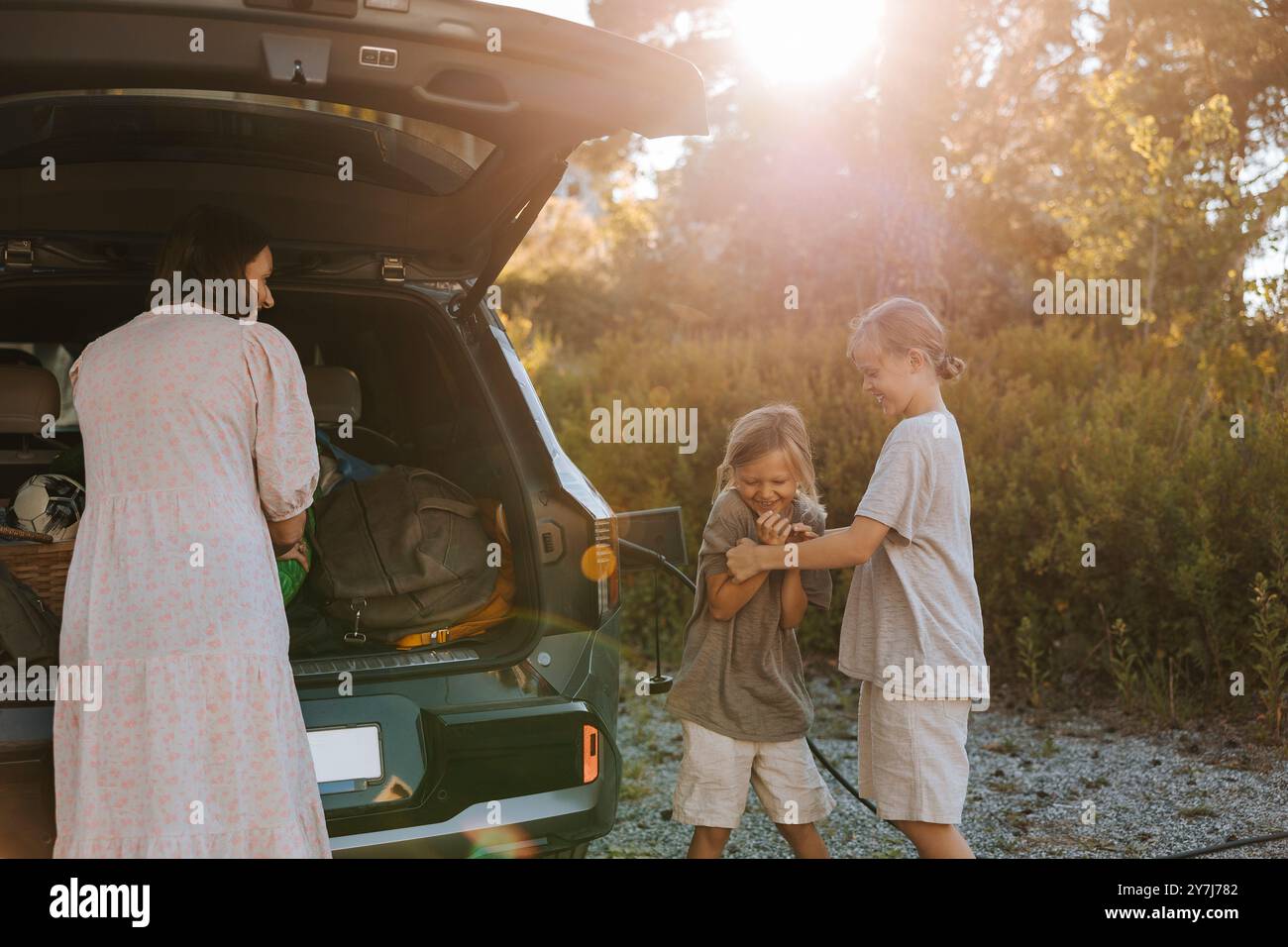 Playful boys with mother loading luggage in electric car trunk on ...