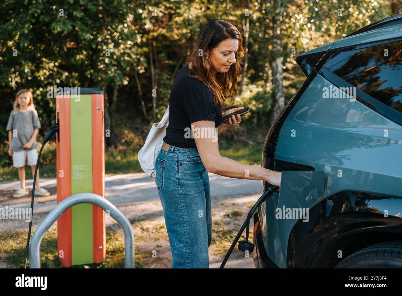 Side view of woman removing electric plug after charging car at station ...