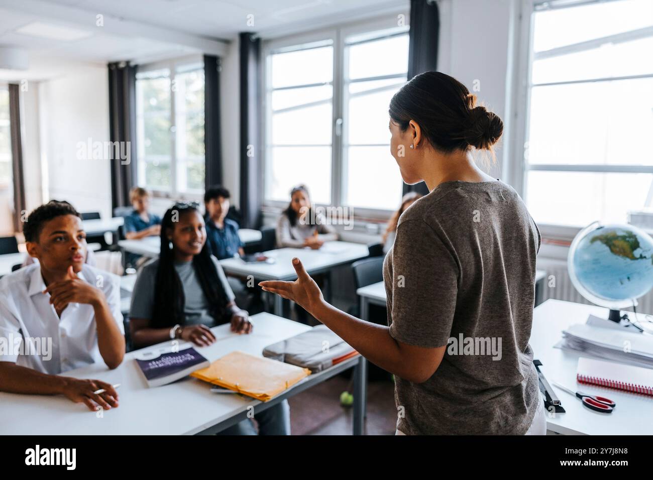 Rear view of female teacher teaching group of male and female students ...