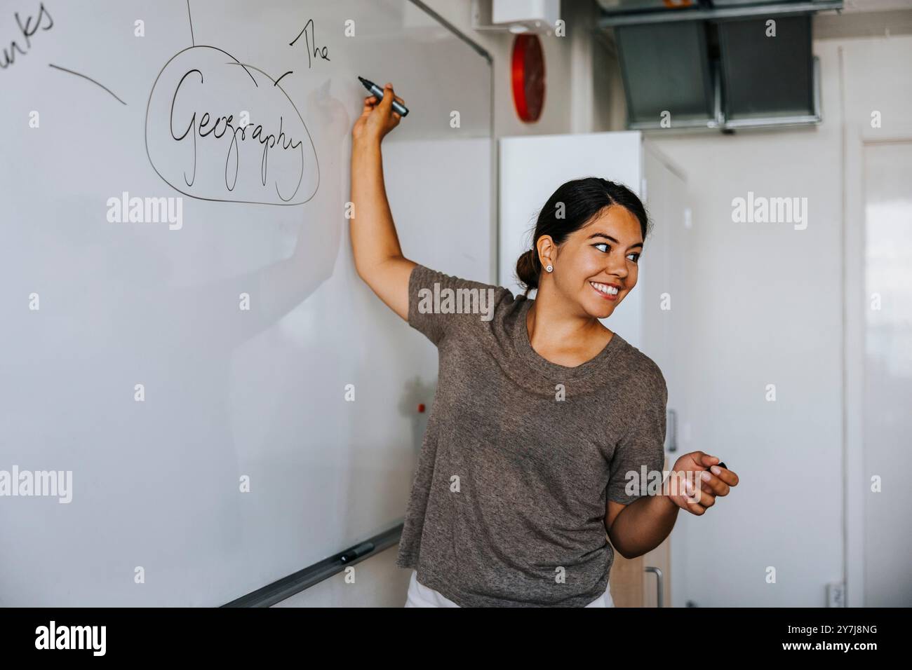 Happy female professor holding felt tip pen while standing near ...