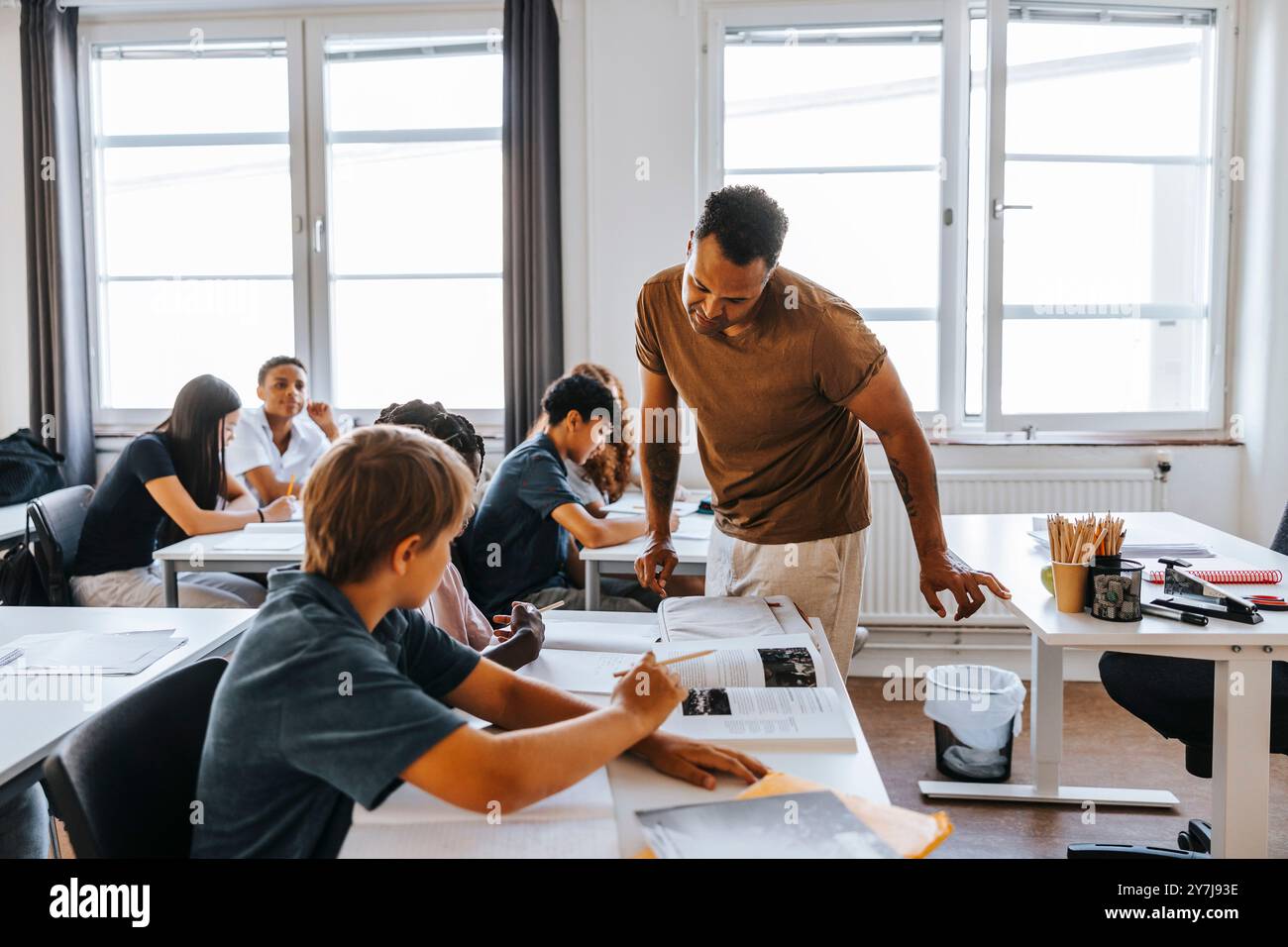 Male teacher assisting junior high student sitting near desk in ...