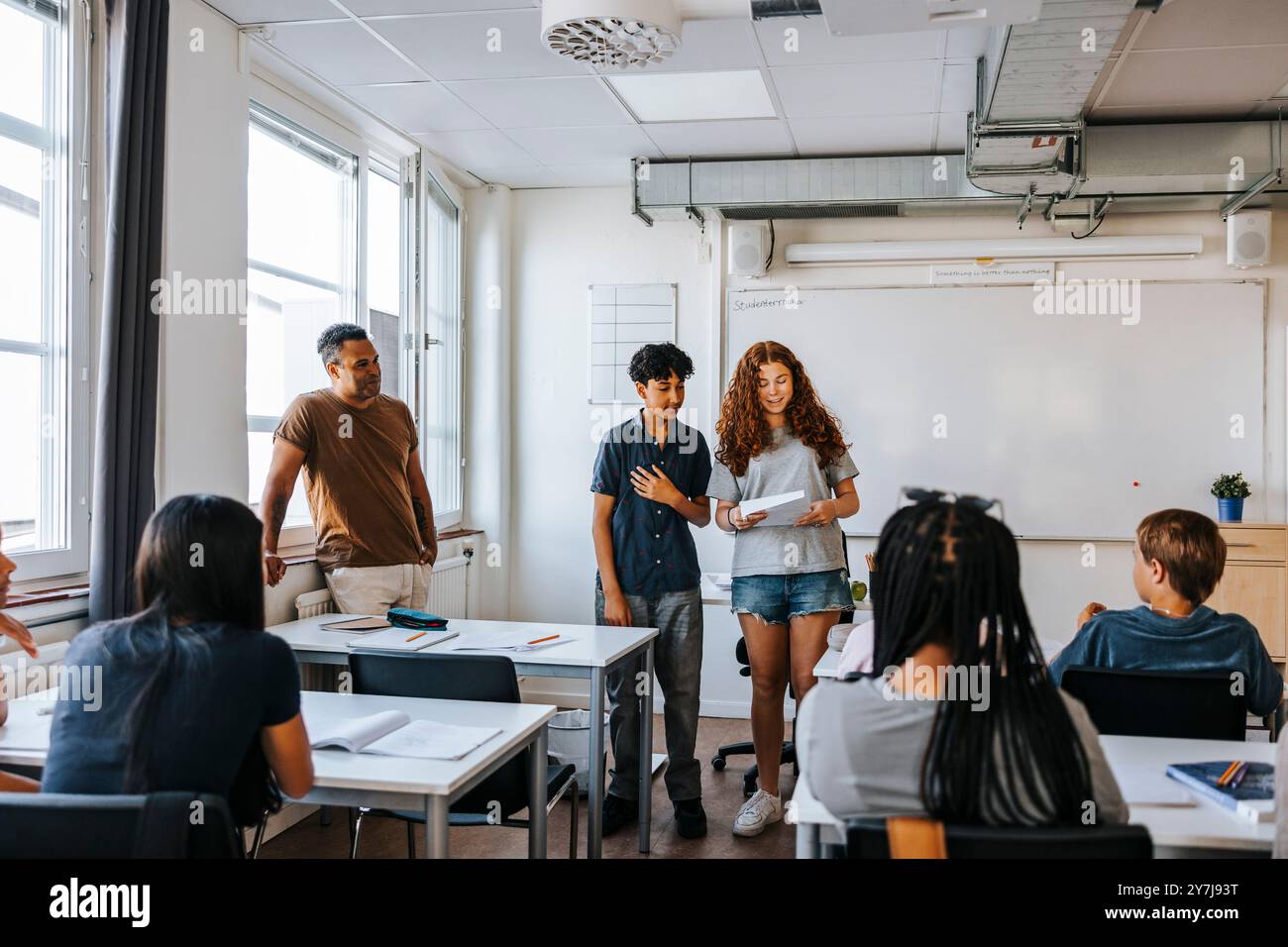 Male professor standing near teenage girl and boy reading in front of ...