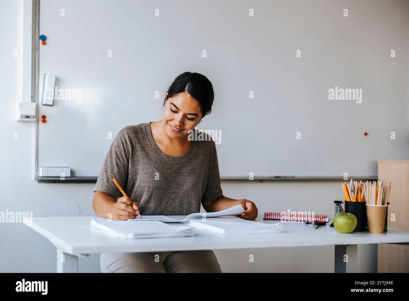 Smiling professor checking test papers while sitting near table in ...