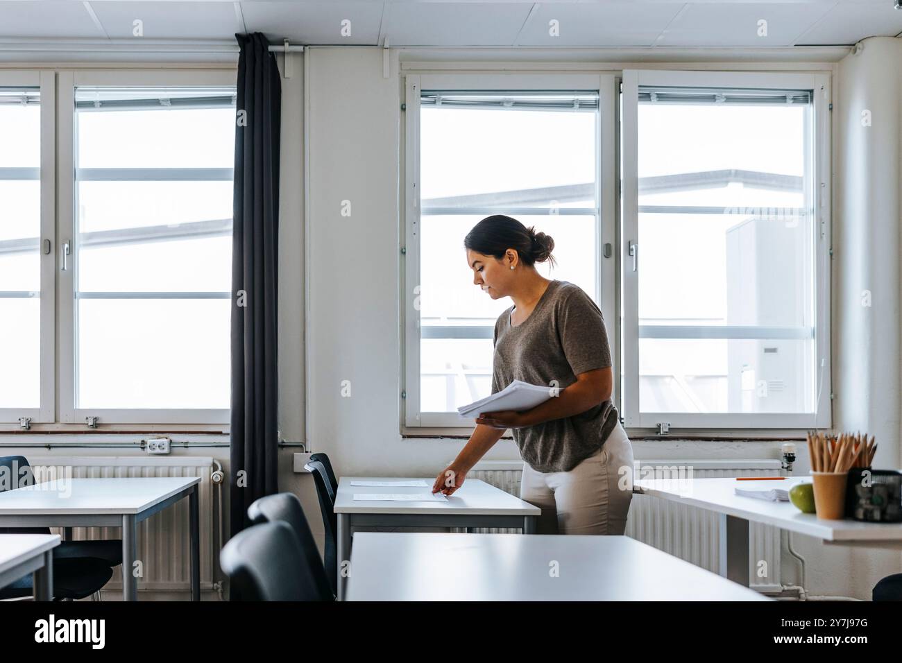 Female professor keeping test papers on desk while standing in ...