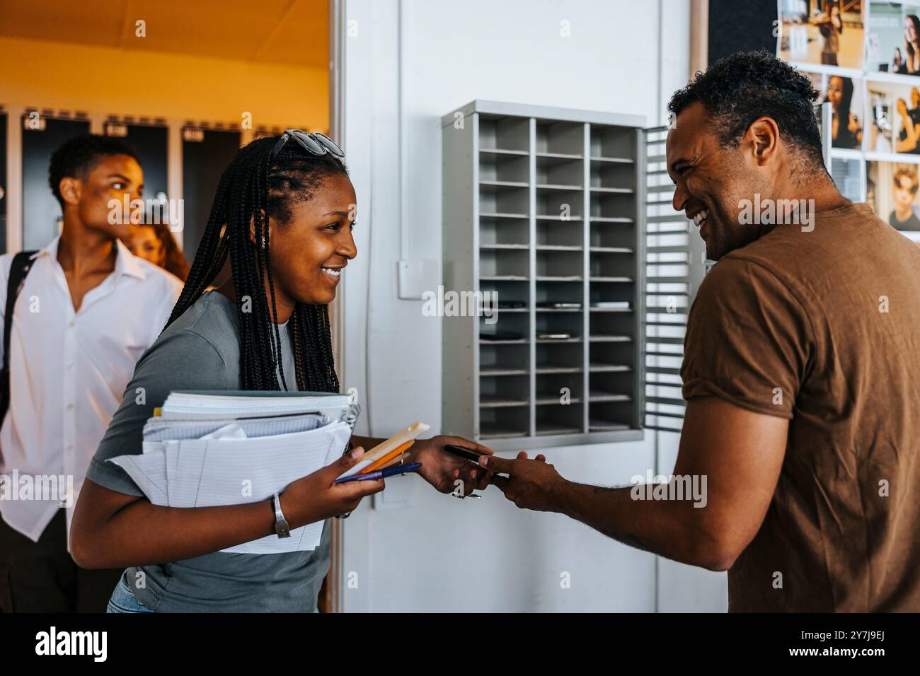 Happy male teacher collecting smart phone from teenage girl standing ...