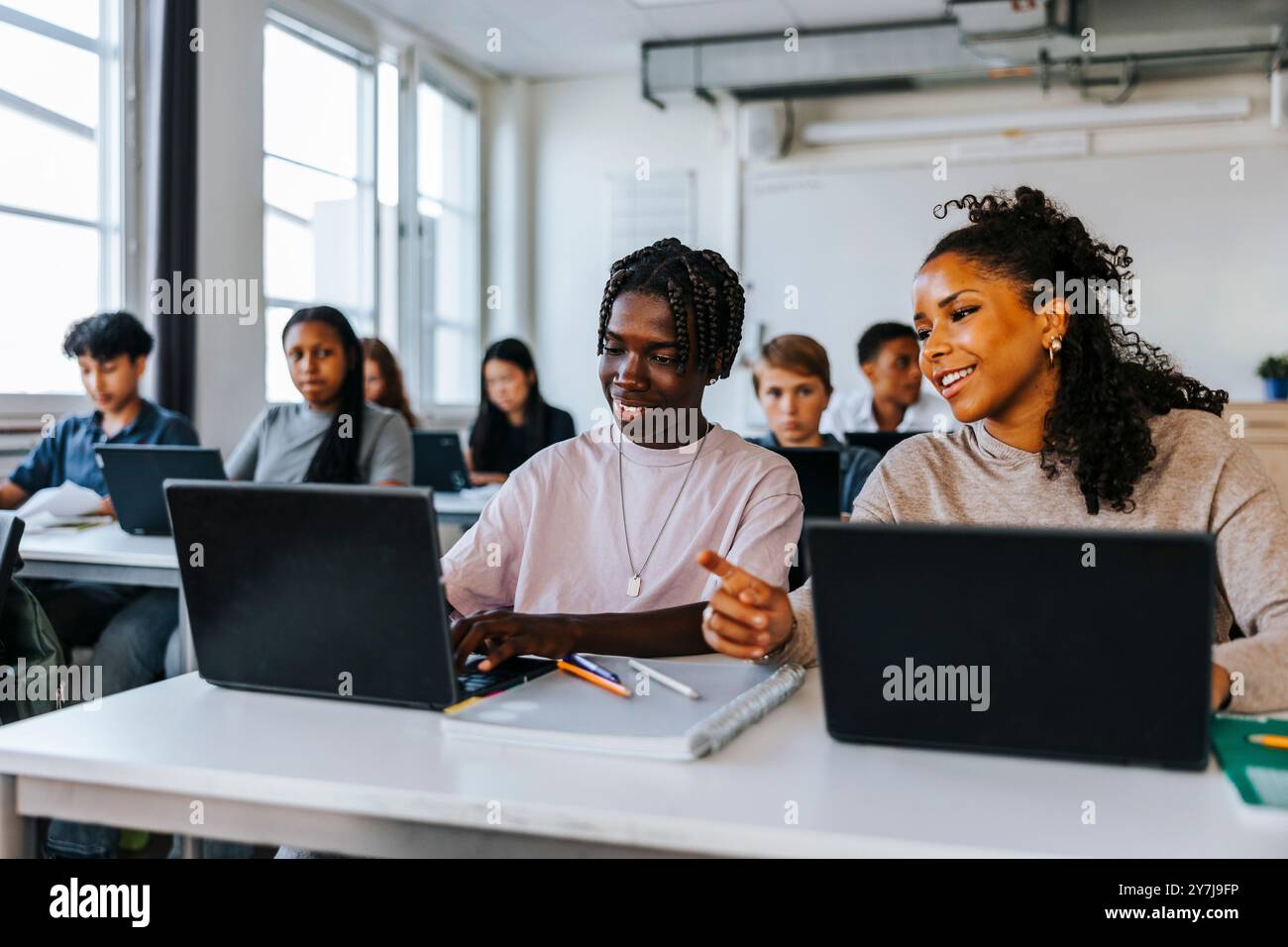 Smiling teenage girl sitting with male classmate while studying on ...