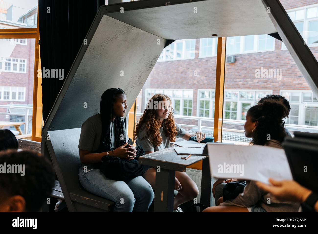 Female students studying while sitting in hexagon structure at school ...