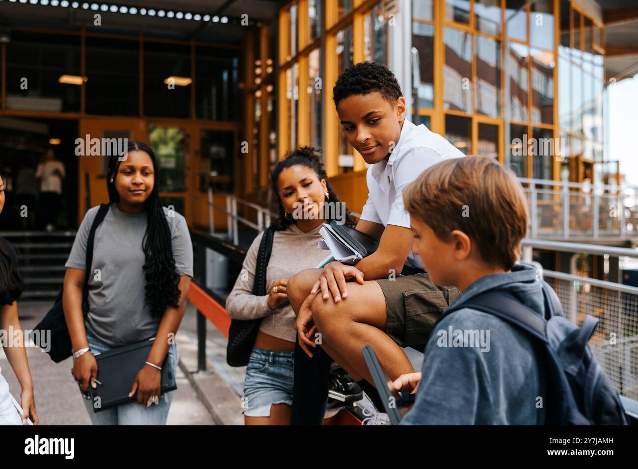 Male and female students discussing while standing at balcony of junior ...