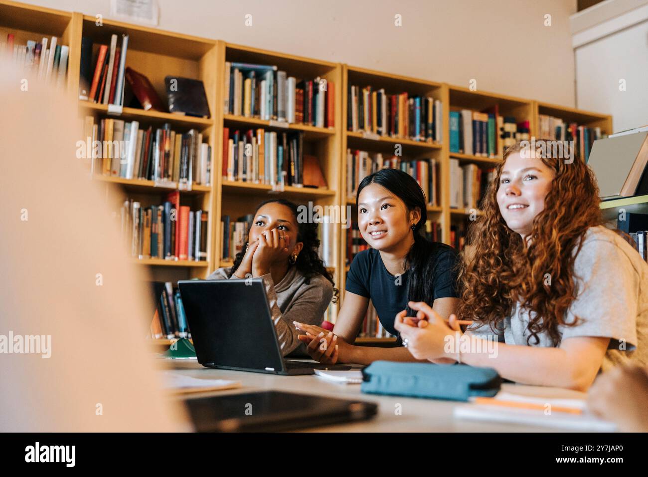 Female junior high students sitting with laptop in library at school ...