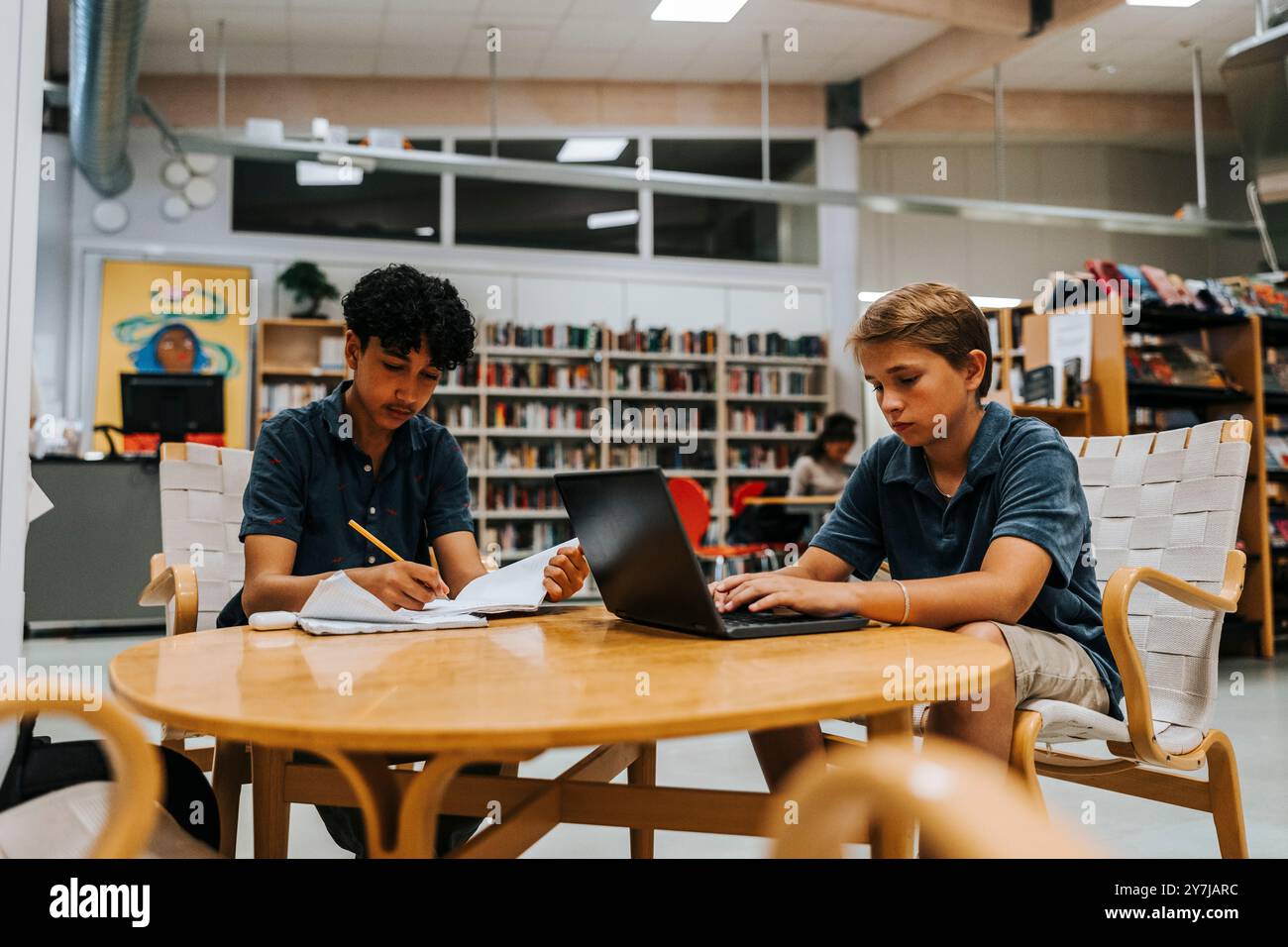 Focused male students studying while sitting near table in library at ...