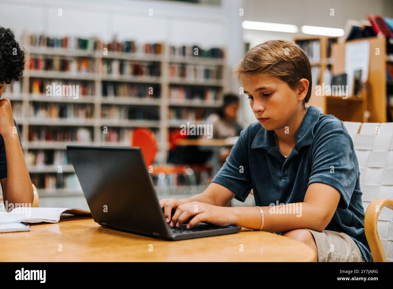 Focused teenage boy studying on laptop while sitting near table in ...