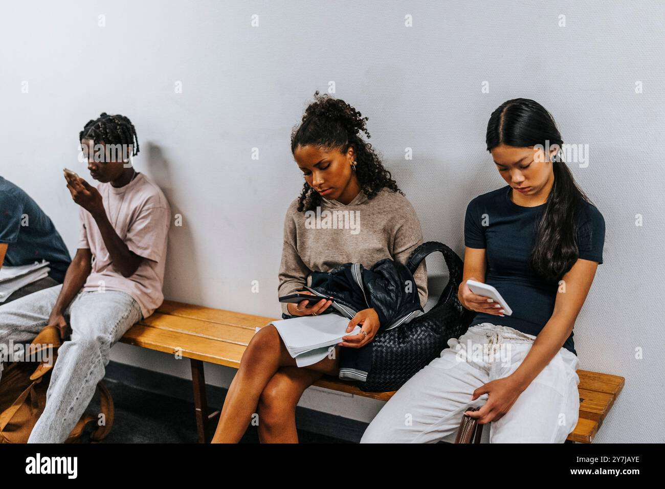 Male and female students using smart phones while sitting on bench near ...