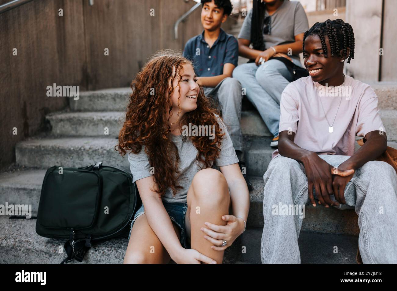 Happy teenage girl sitting with friends on stairs of junior high school ...