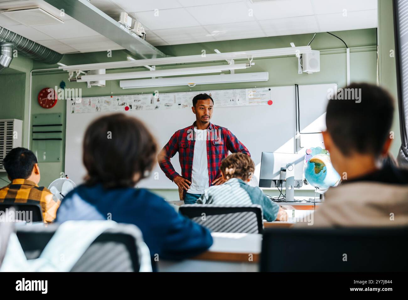 Male teacher with arms akimbo teaching group of students sitting in ...
