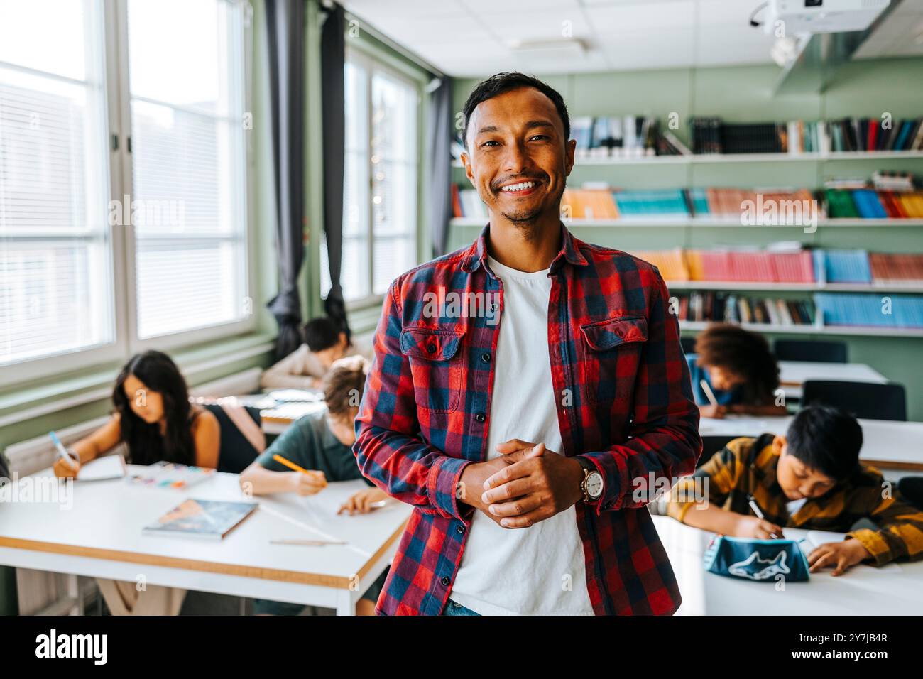 Portrait of smiling male professor with hands clasped standing in ...