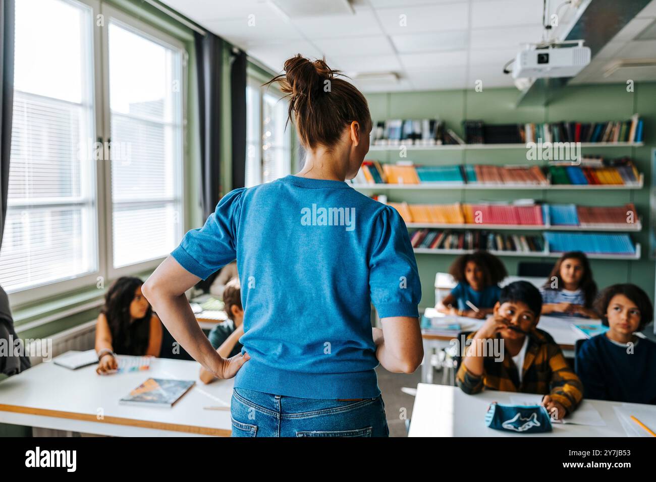 Rear view of female teacher with hand on hip teaching group of ...