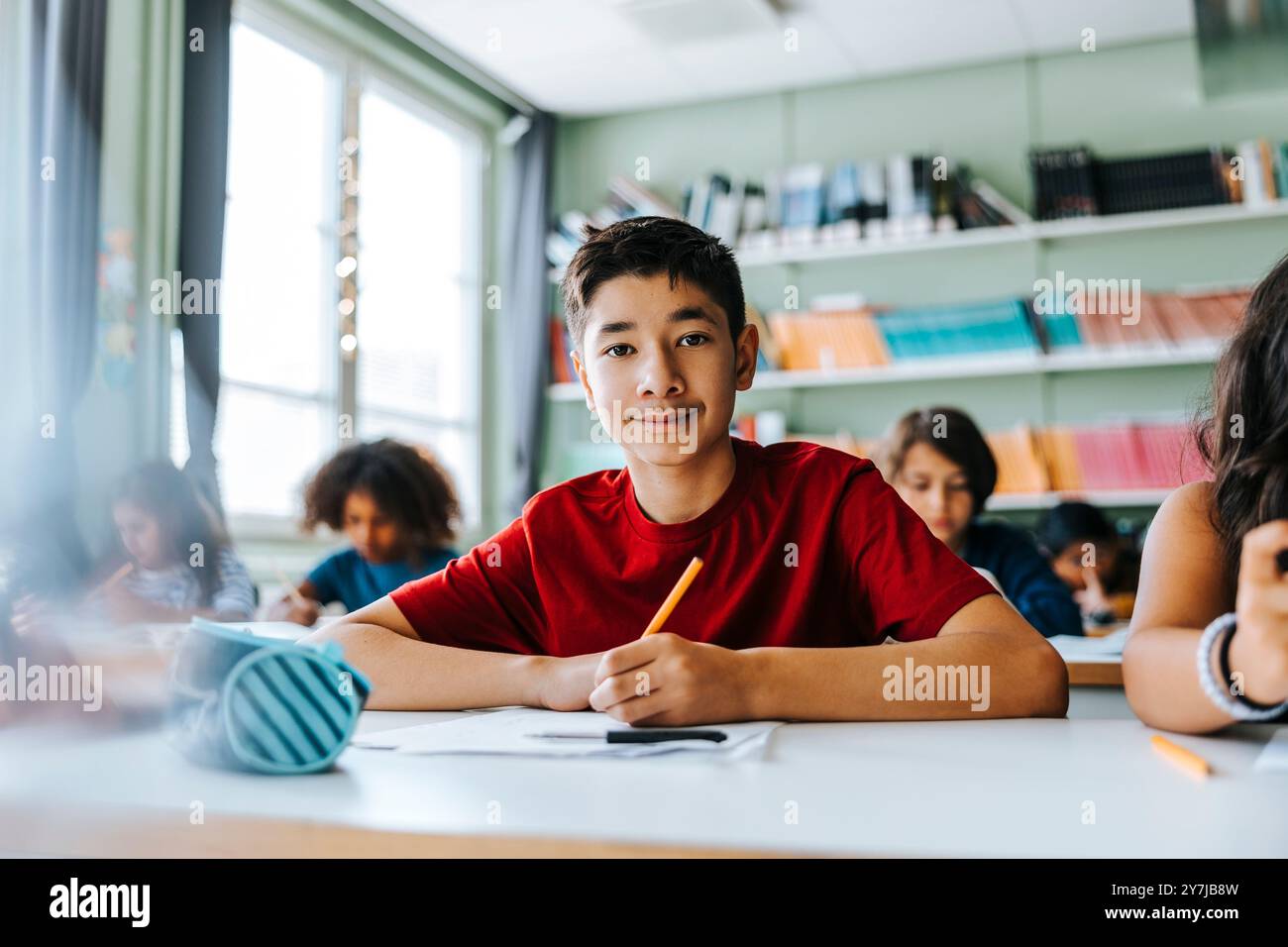 Portrait of boy sitting in classroom with classmates at elementary ...