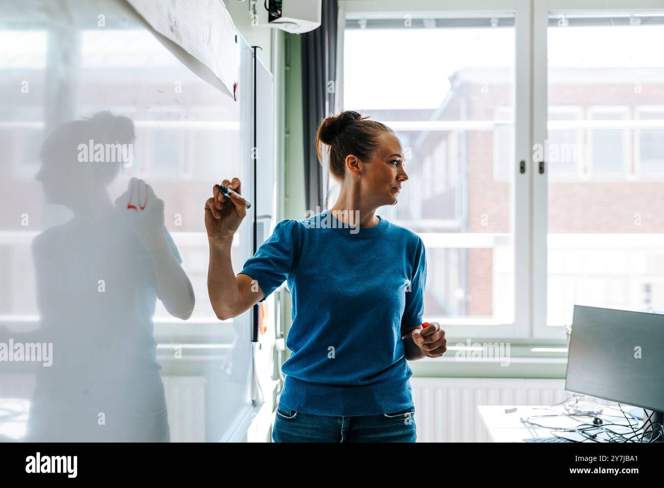 Female professor holding felt tip pen while standing near whiteboard in ...