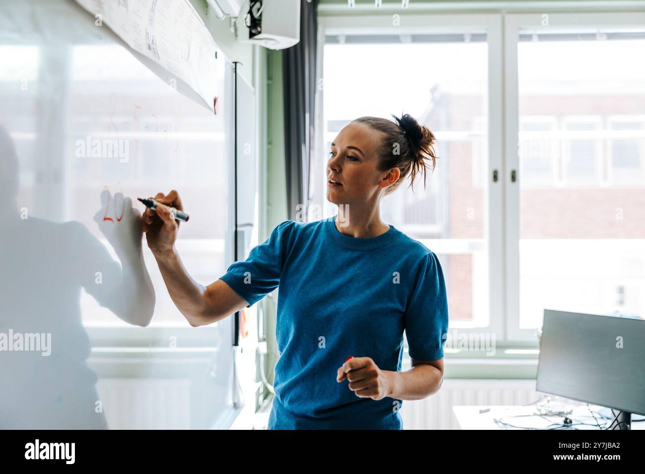 Female teacher writing on whiteboard with felt tip pen while standing ...