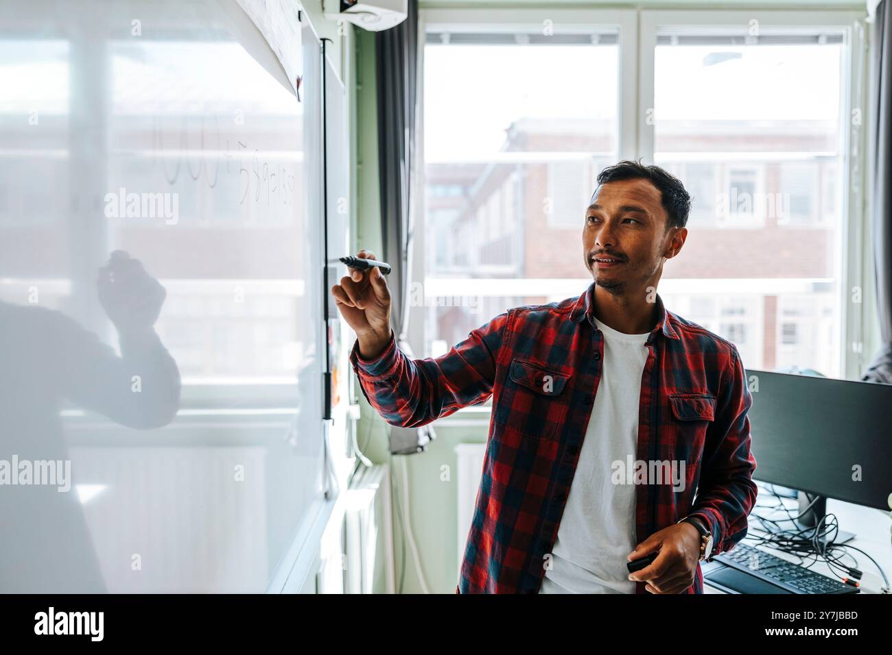 Male teacher writing on whiteboard with felt tip pen while standing in ...