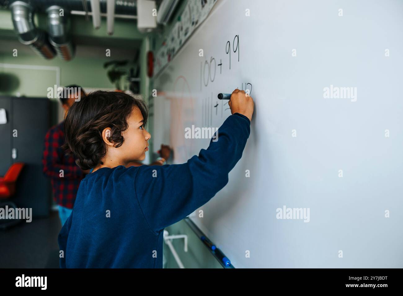 Side view of boy solving mathematics equation on whiteboard in class at ...