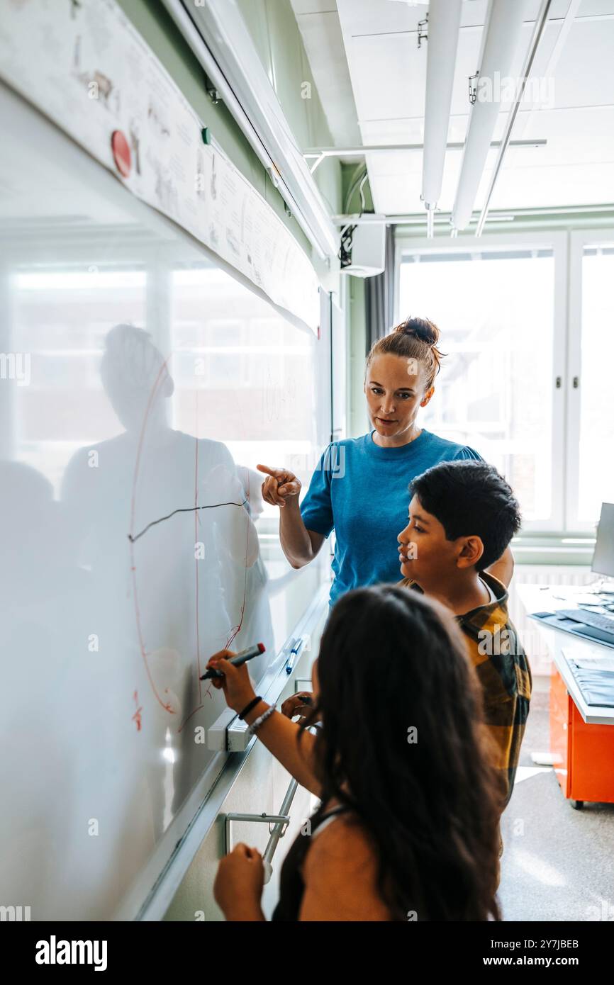 Female teacher assisting students drawing diagram on whiteboard in ...