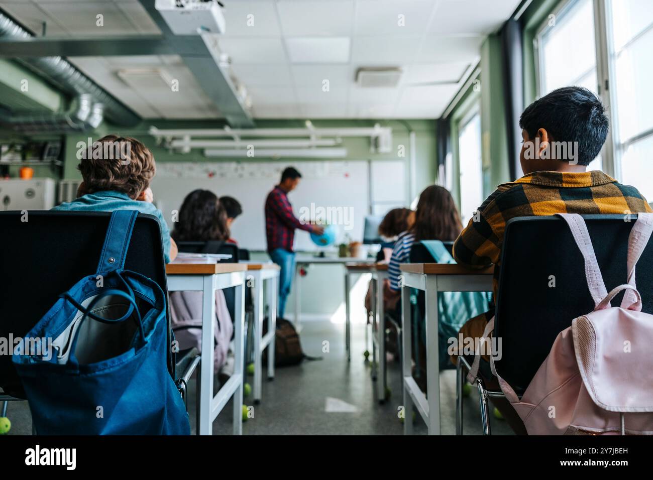 Backpacks hanged on chair with students sitting in classroom at ...