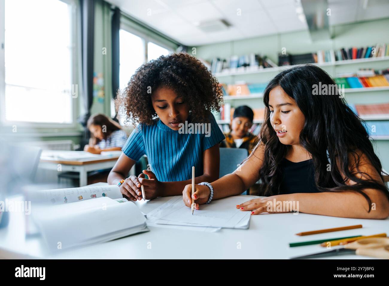 Female classmates writing while studying together and sitting near desk ...