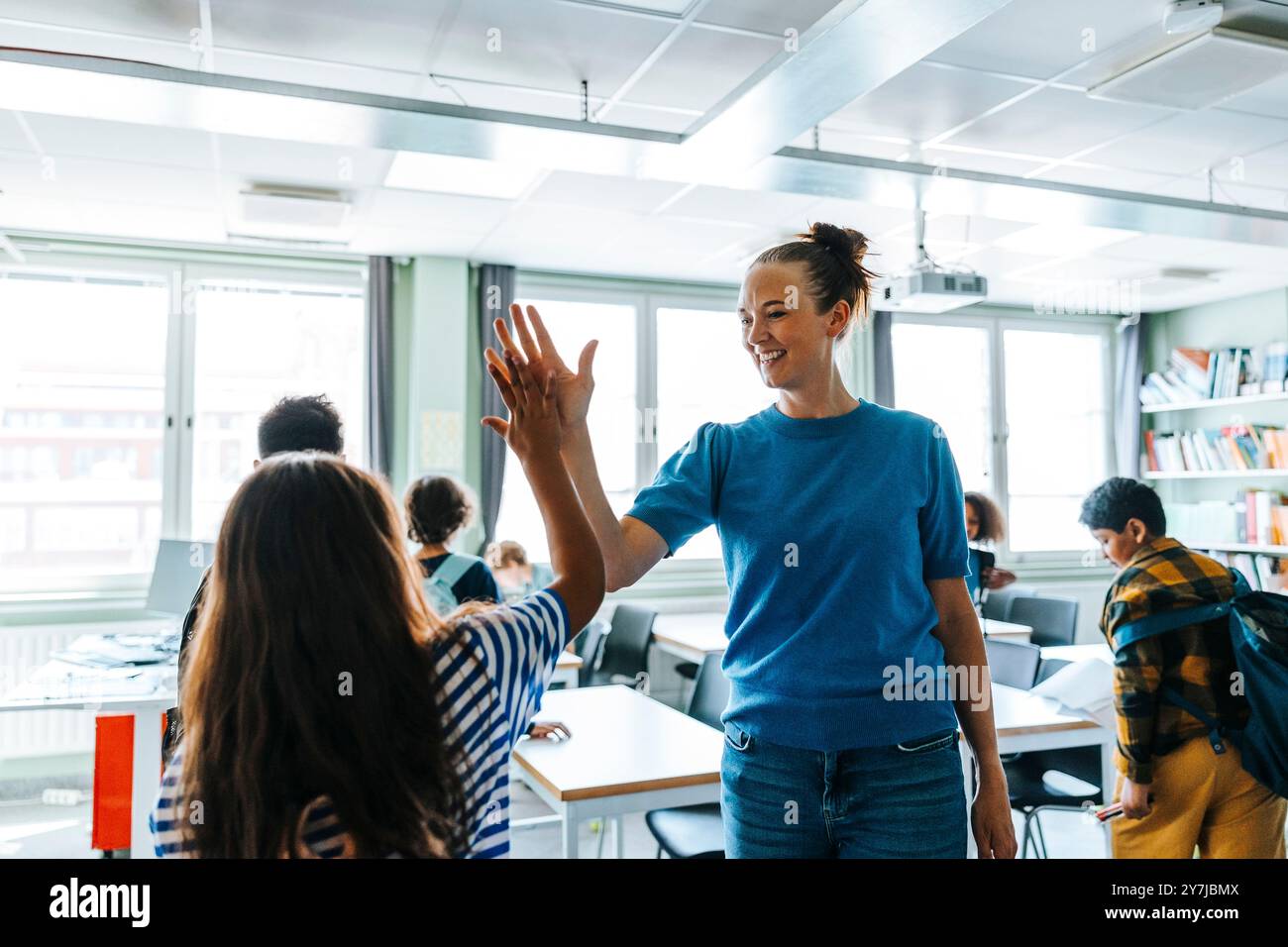 Happy female teacher giving high-five to female student while standing ...