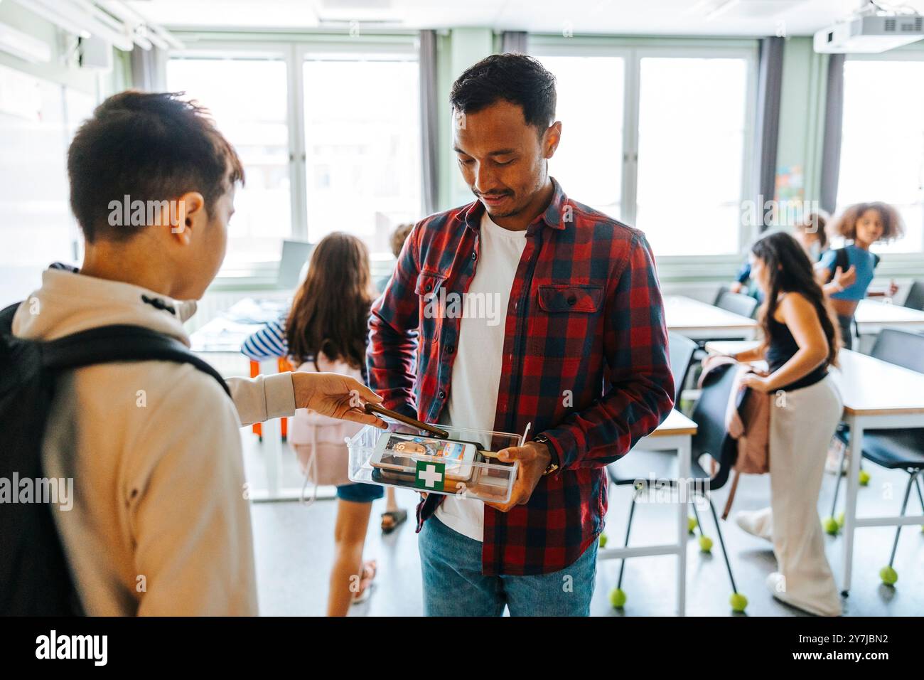 Male professor collecting smart phones of students while standing in ...